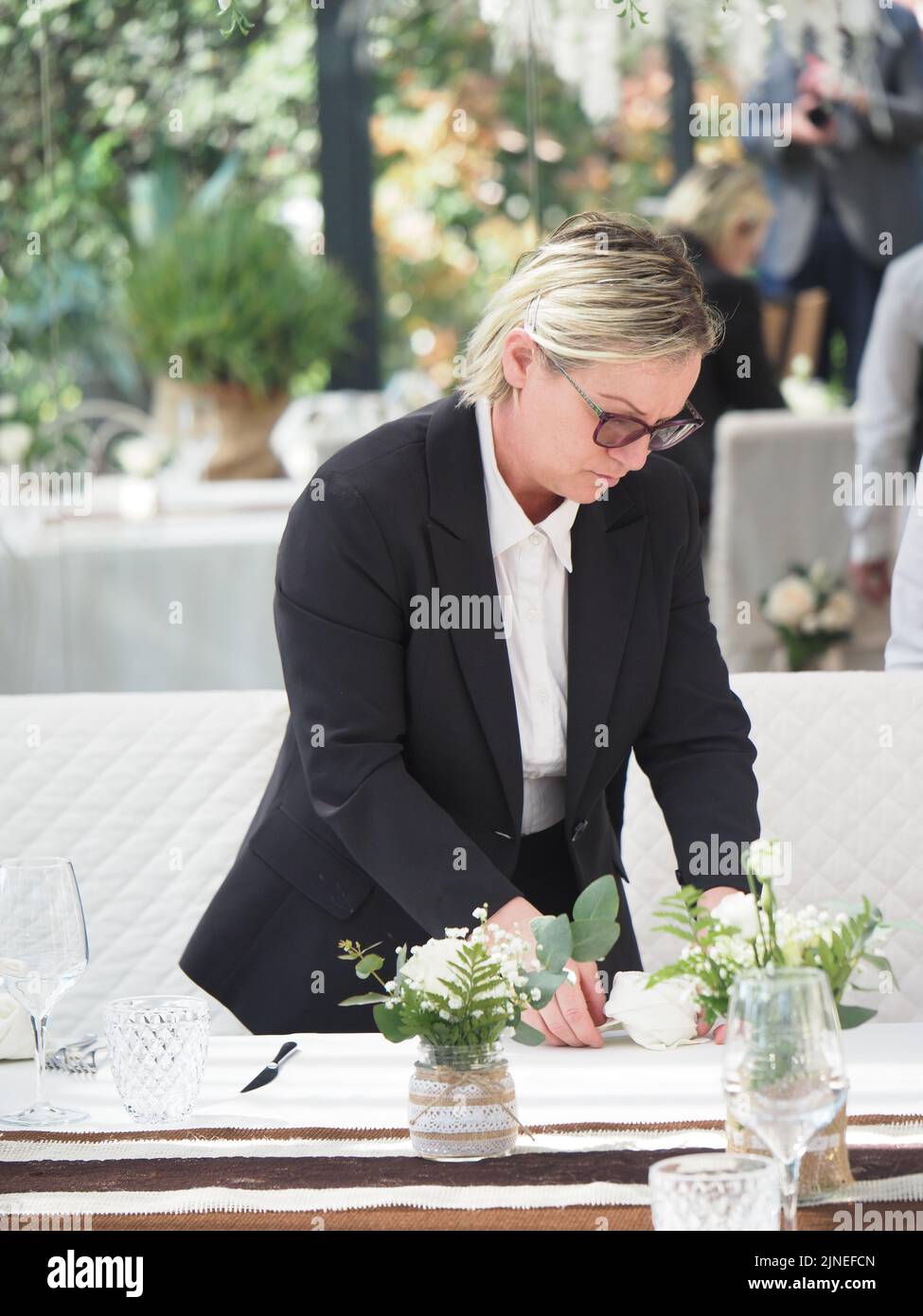 A vertical shot of a female waiter setting up a table at an outdoor ...