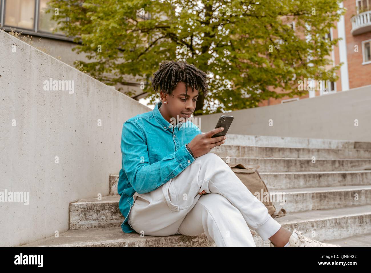Dark-skinned man looking at smartphone sitting on steps Stock Photo - Alamy