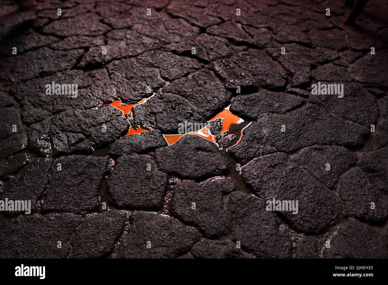 A top view of a puddle reflecting an orange light on a paved street ...