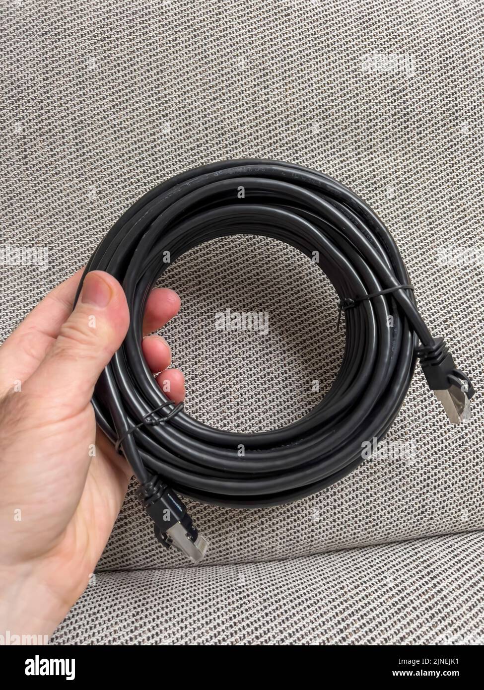 Male hand holding black lan cable with plug on gray fabric background ...