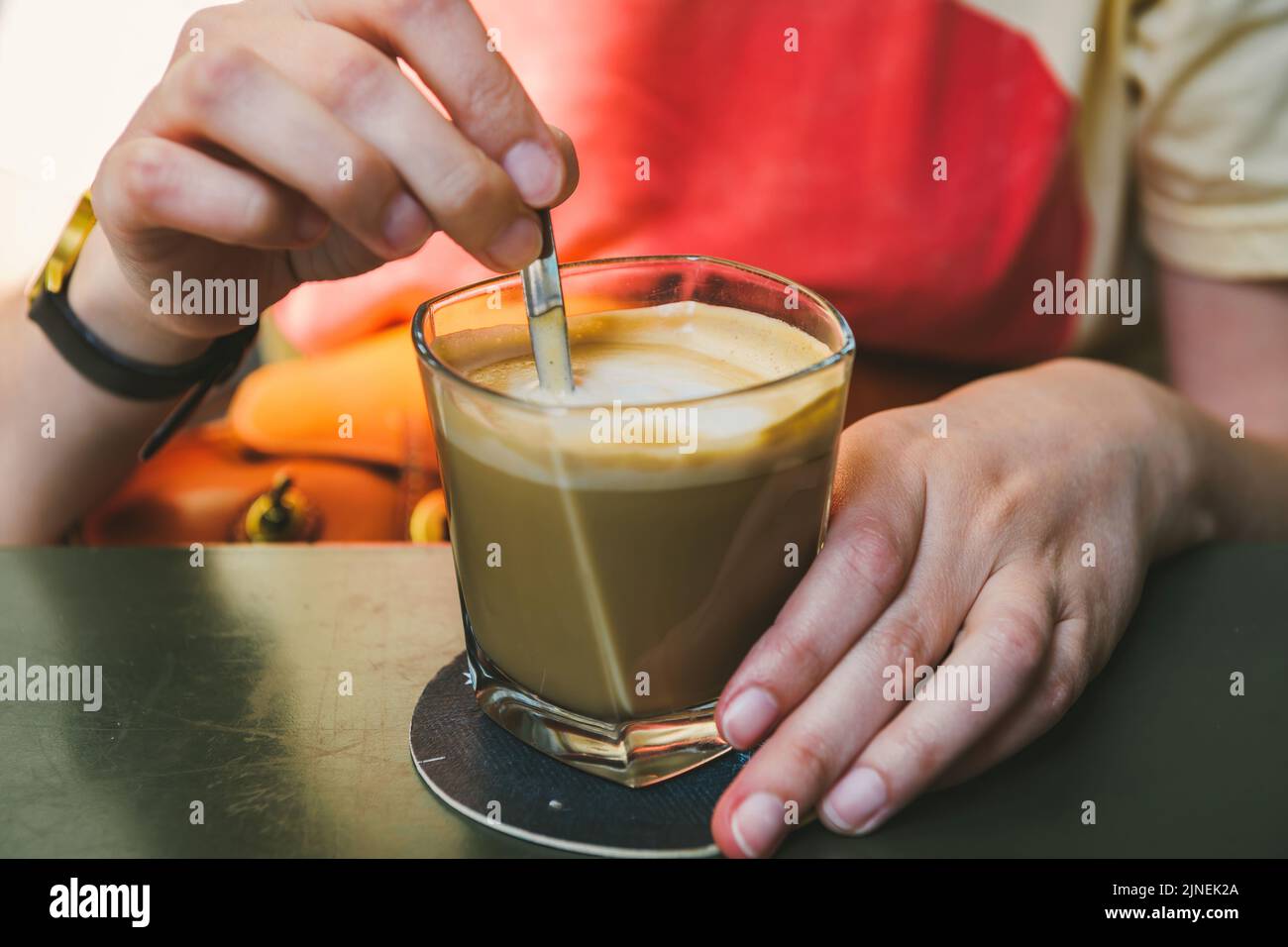 Front view of woman hands mixing delicious coffee with milk in glass ...