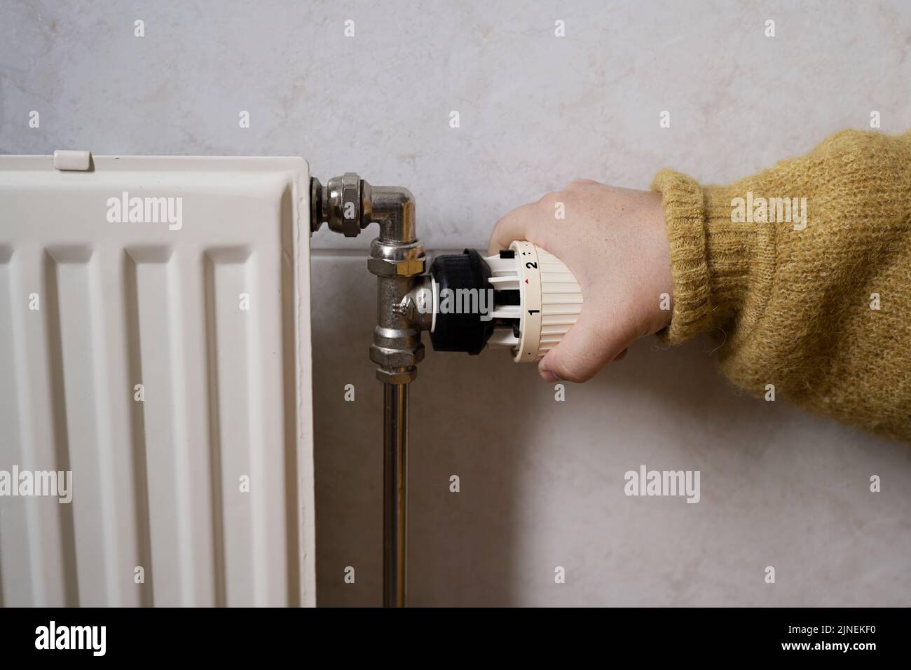 Hand turning off the heating, radiator while wearing a warm yellow ...