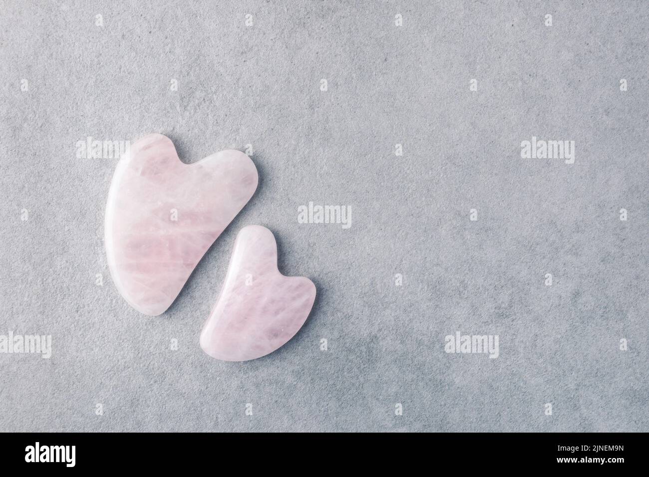 Rose quartz gua sha stones of different size on grey stone background ...