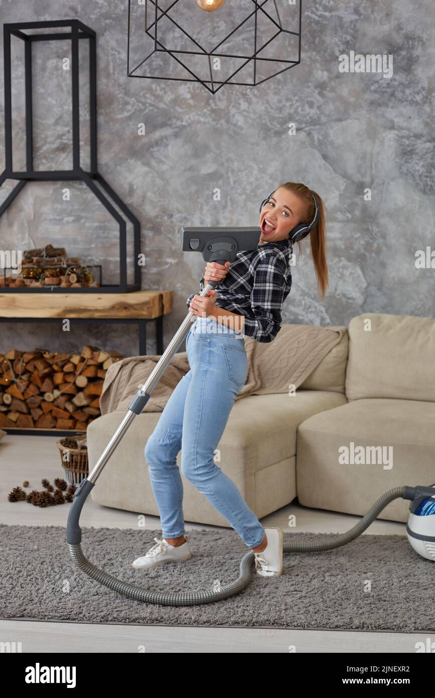Cheerful young woman enjoying solo singing with vacuum cleaner while ...
