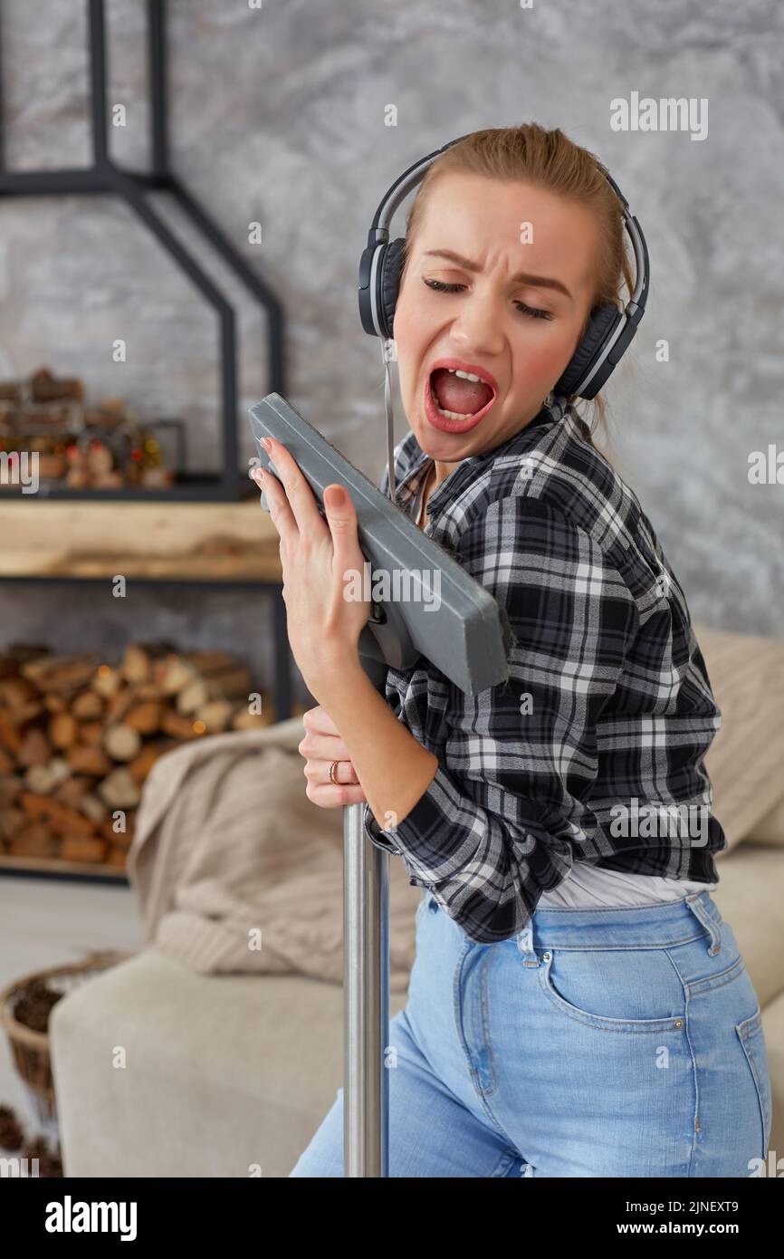 Cheerful young woman enjoying solo singing with vacuum cleaner while ...