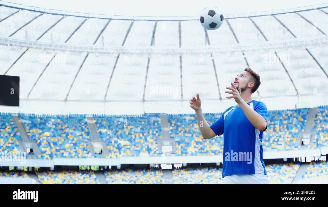 sportive football player in blue uniform bouncing ball with head on ...
