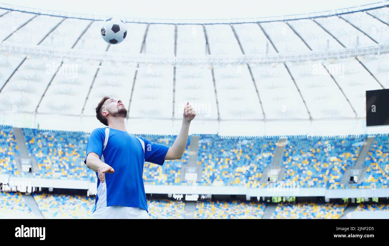 football player in blue t-shirt bouncing ball with head on stadium ...