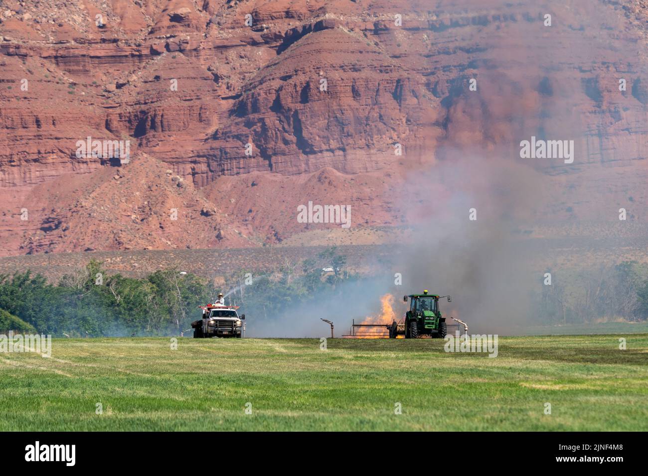 A tractor pulls a propane burner to burn weeds in an hay field after ...