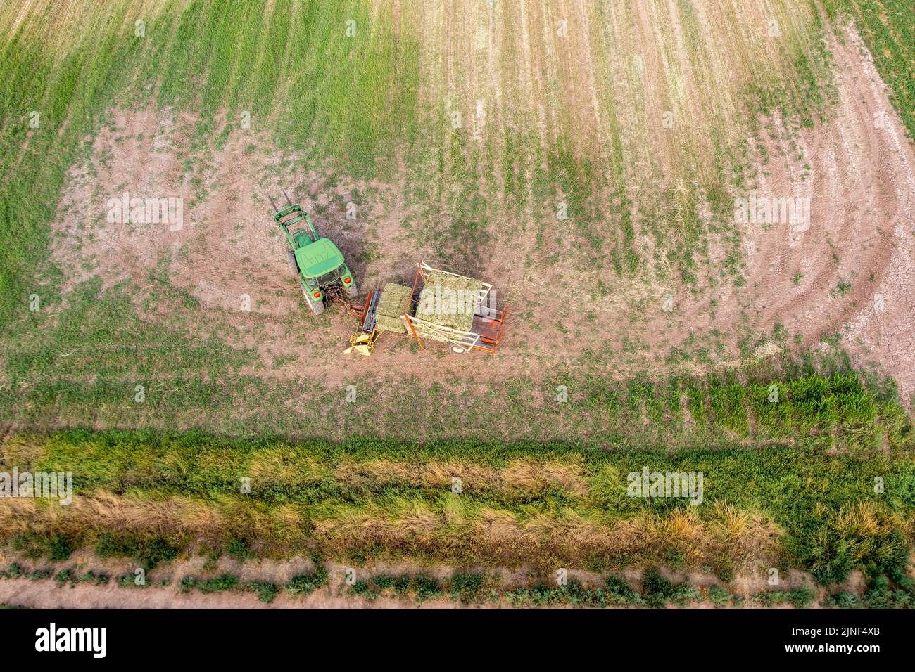An aerial view of a rancher collecting hay bales with a tractor and a ...
