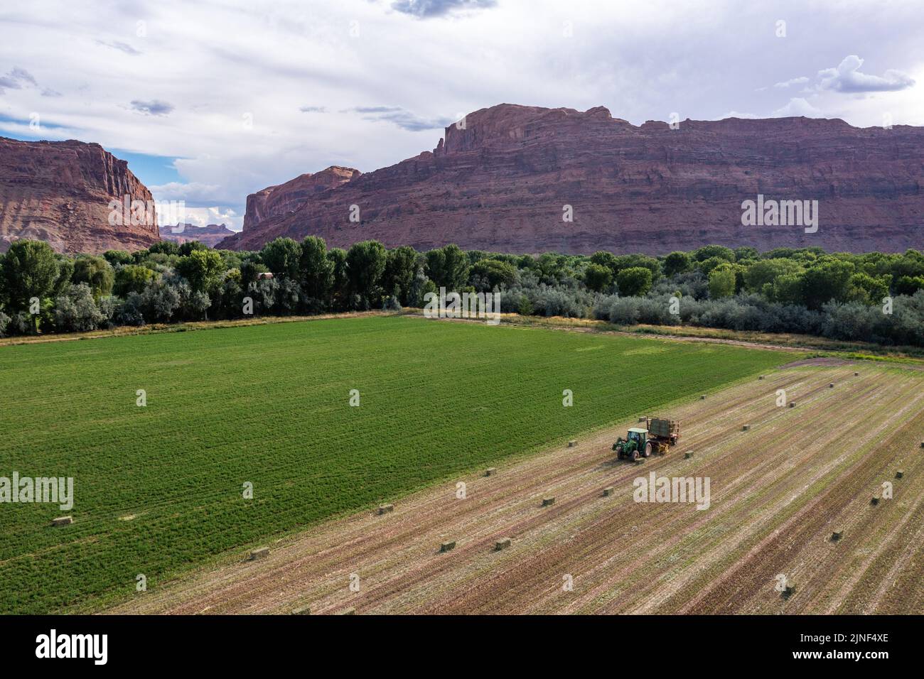 An aerial view of a rancher collecting hay bales with a tractor and a ...