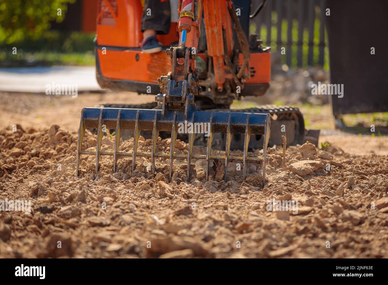 A mini excavator with a rake loosens the ground. landscape preparation ...