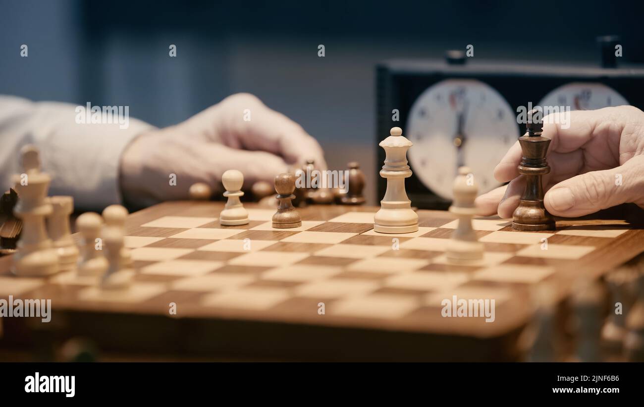 partial view of senior men playing chess on blurred chessboard,stock ...