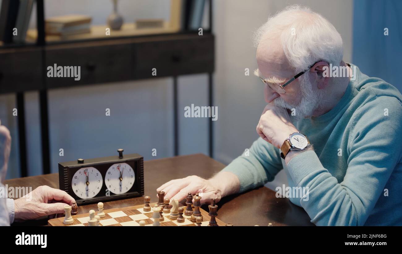 thoughtful senior man moving chess figure while gaming with friend in ...