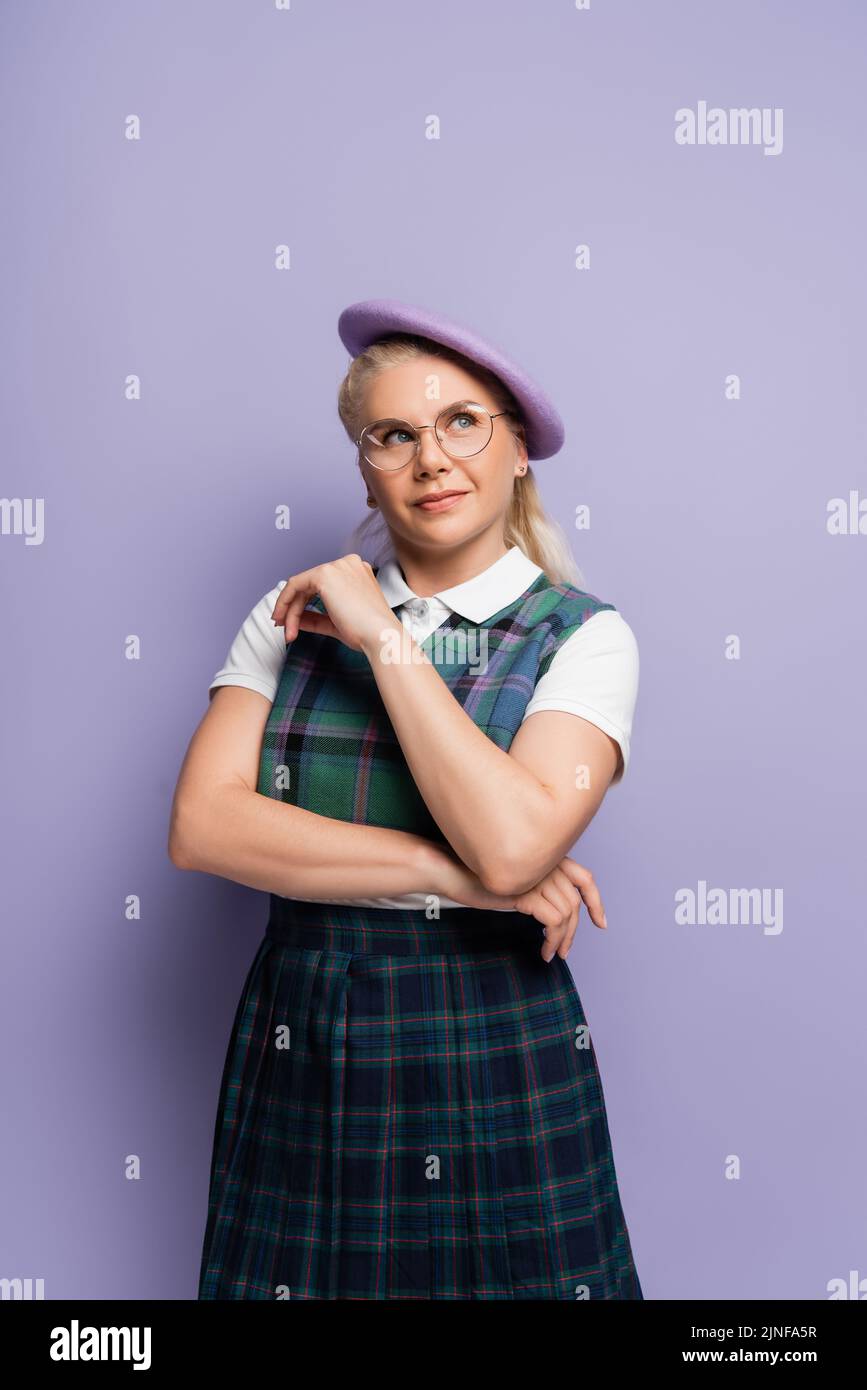 Blonde student in checkered uniform and beret looking away on purple ...