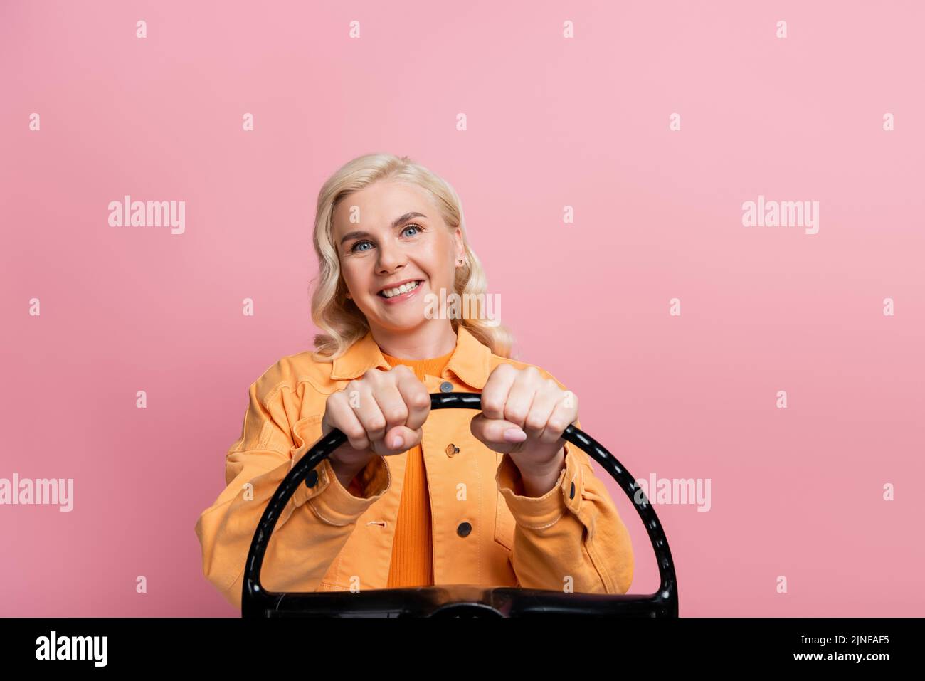 Cheerful blonde driver in jacket holding steering wheel isolated on ...
