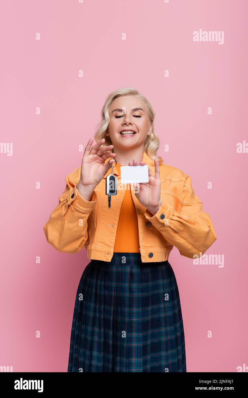 Happy driver holding car key and empty driving license isolated on pink ...