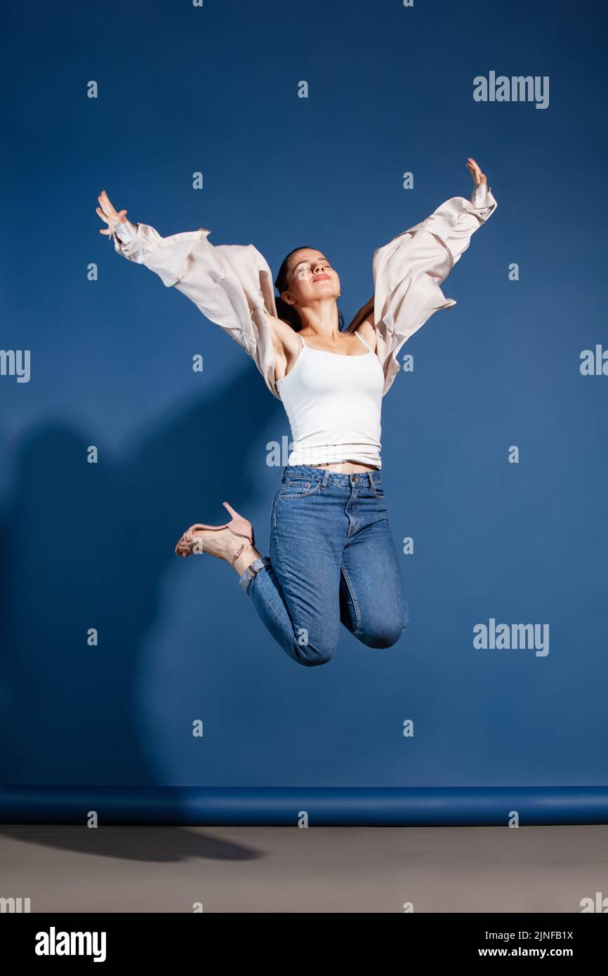Portrait of young woman posing, cheerfully jumping isolated over blue ...