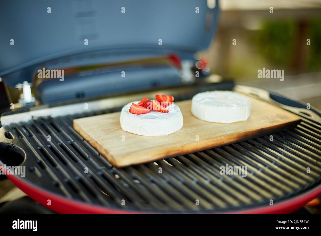 Woman hand put strawberry on grill camembert cheese outdoor, on ...