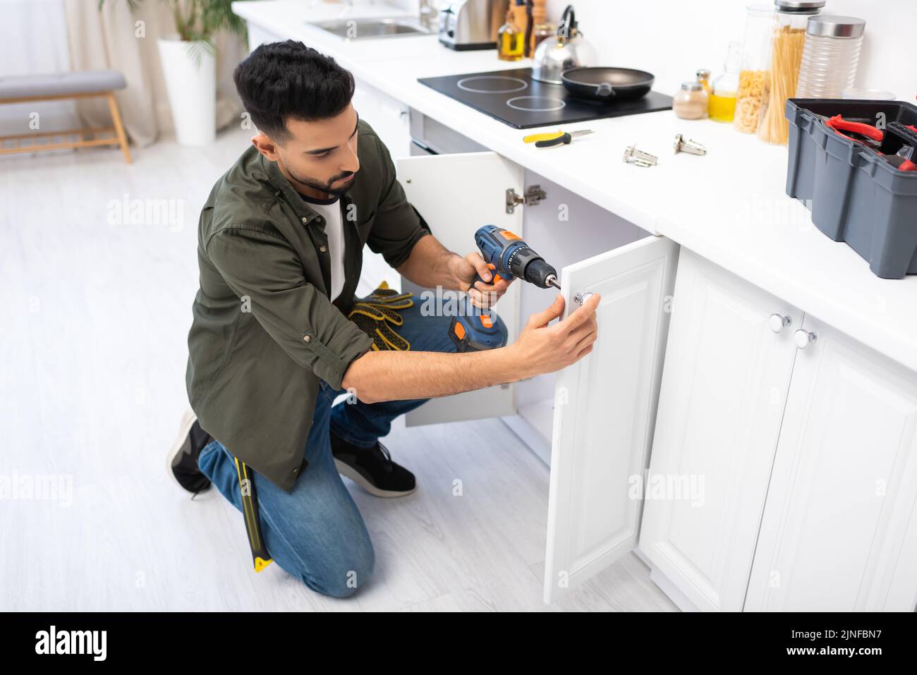 Arabian man with electric screwdriver fixing cabinet under worktop in ...