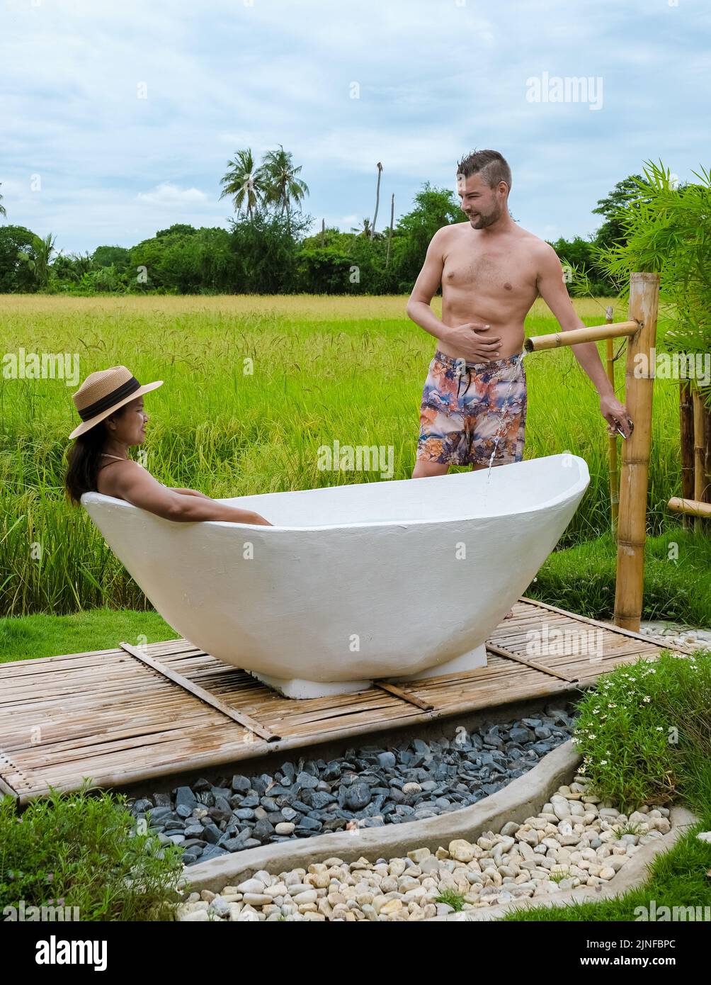 a couple of men and women in a white bathtub outside looking out over a green rice field, men ...