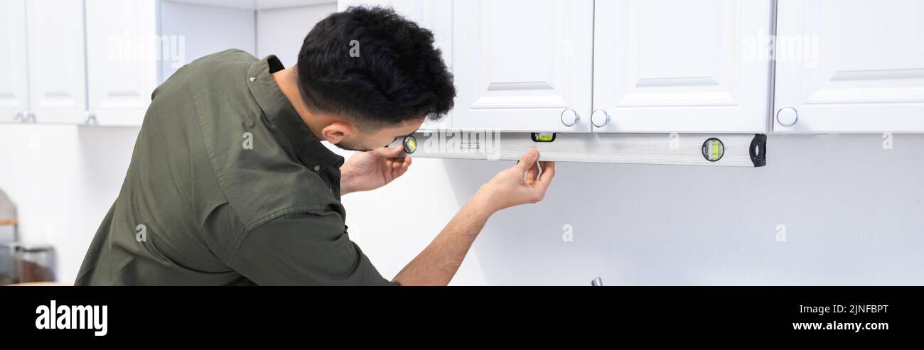 Arabian man measuring kitchen cupboard with spirit level at home ...
