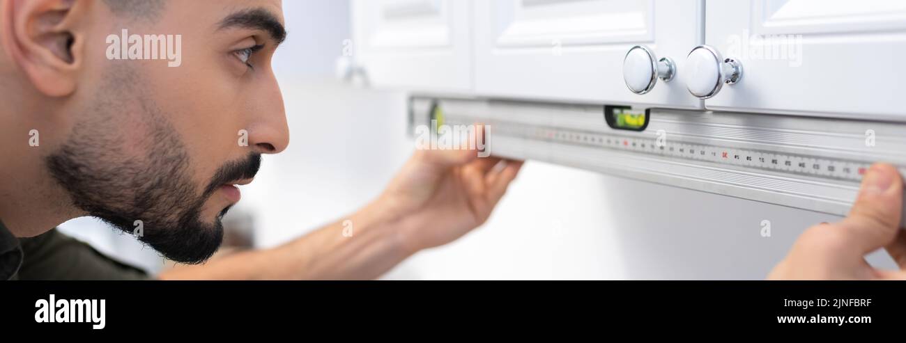 Side view of arabian man measuring kitchen cupboard with spirit level ...