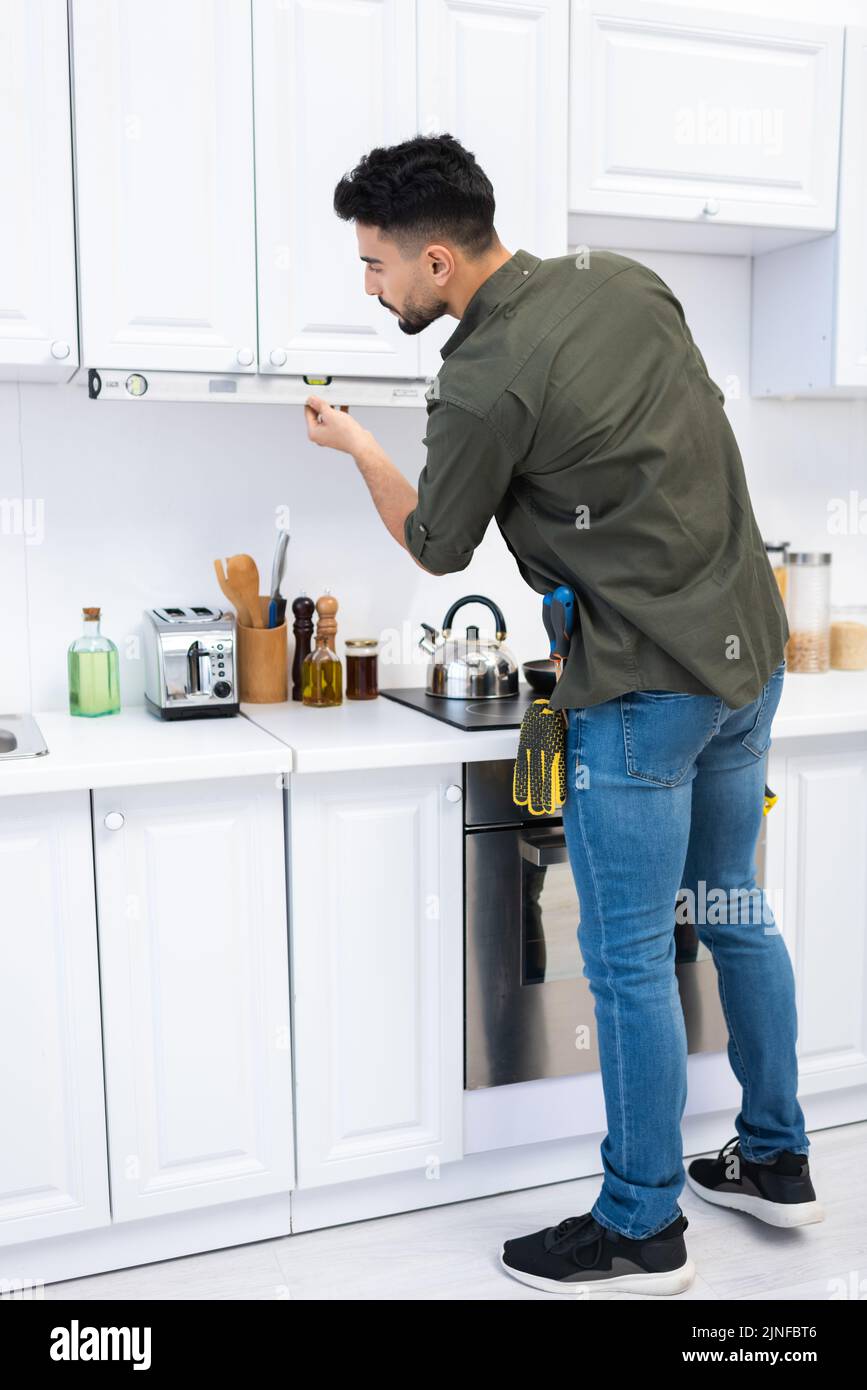 Side view of arabian man with spirit level measuring kitchen cupboard ...