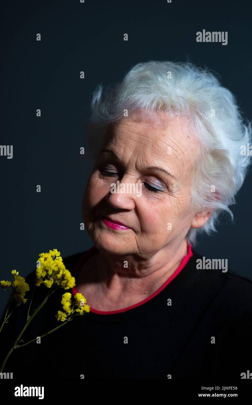 authentic portrait of grandmother holding yellow flower on dark gray ...