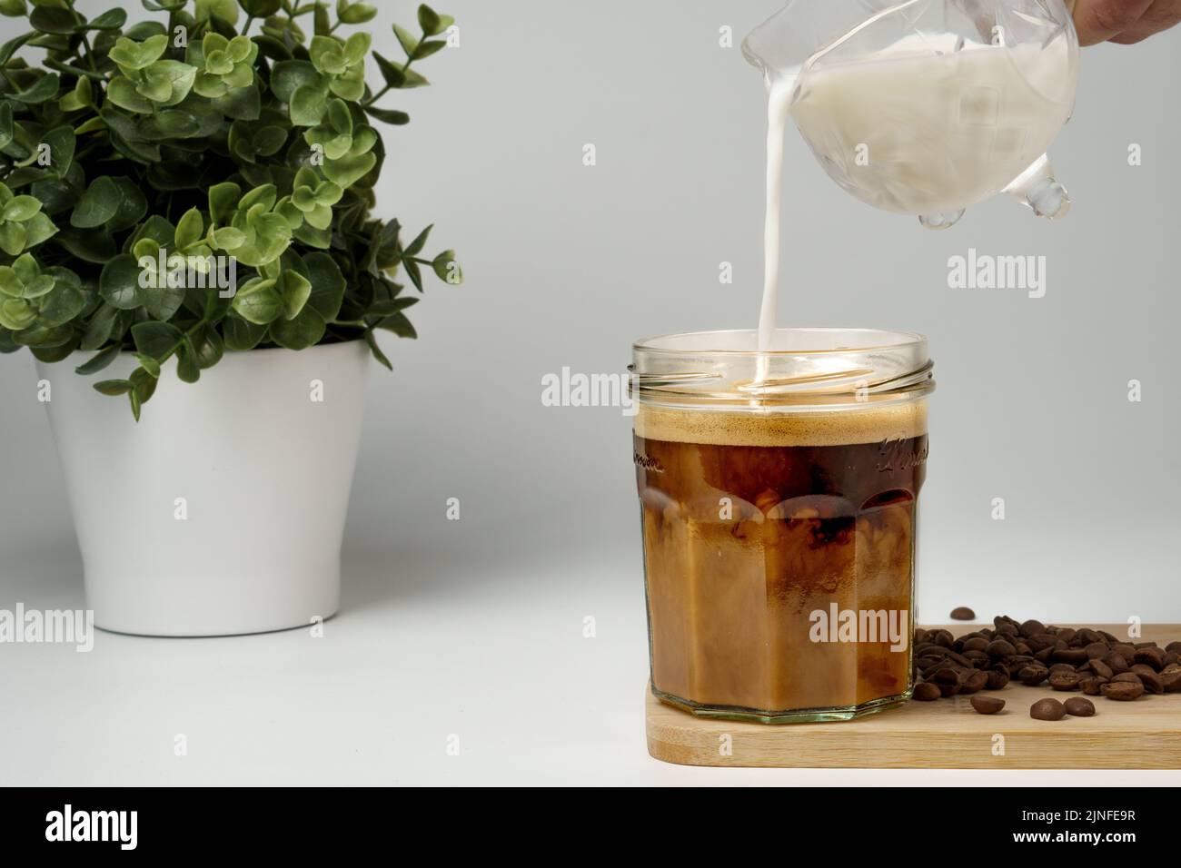 A hand pouring milk into the coffee glass with a white background Stock ...