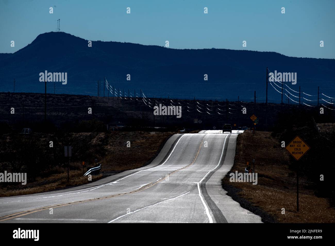 A deserted wavy road with power lines and mountains on the background ...