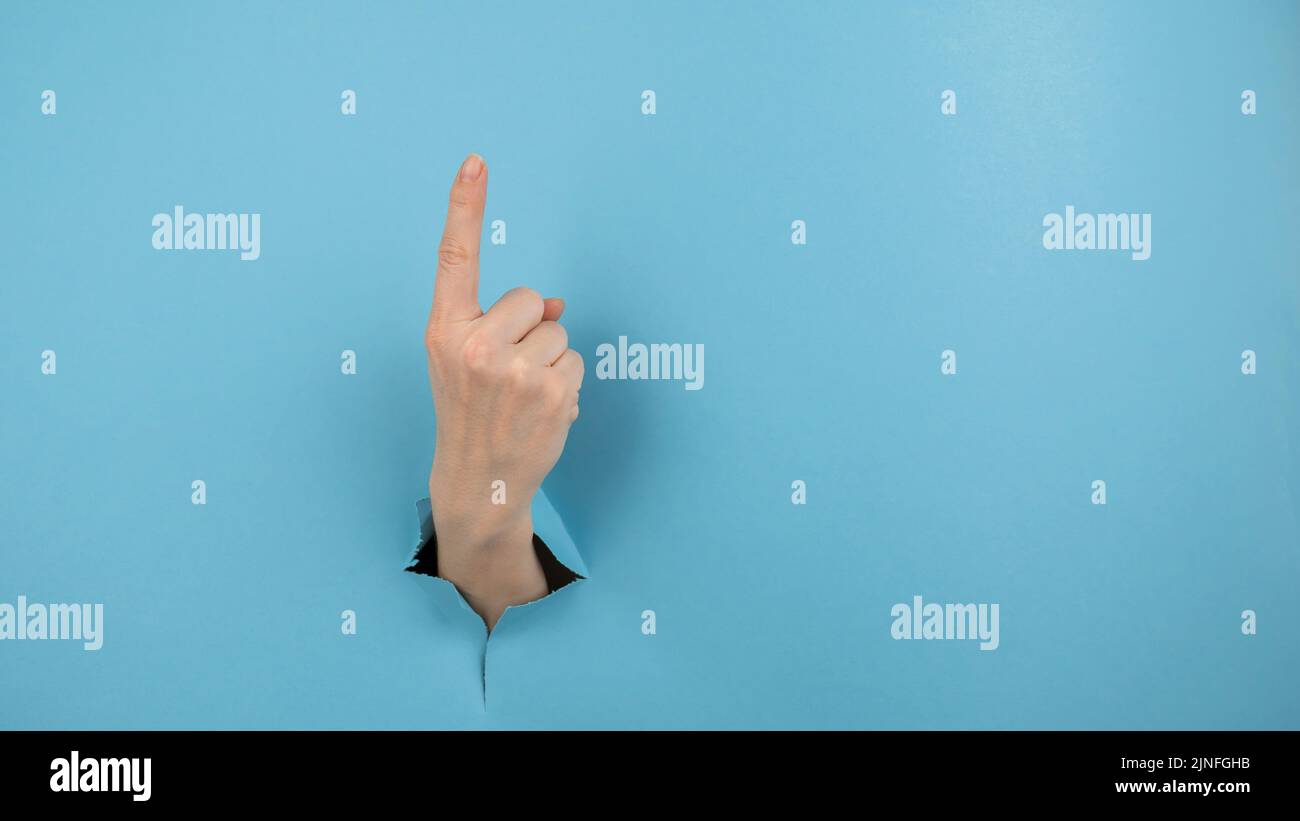 A woman's hand sticking out of a hole from a blue background shows her ...