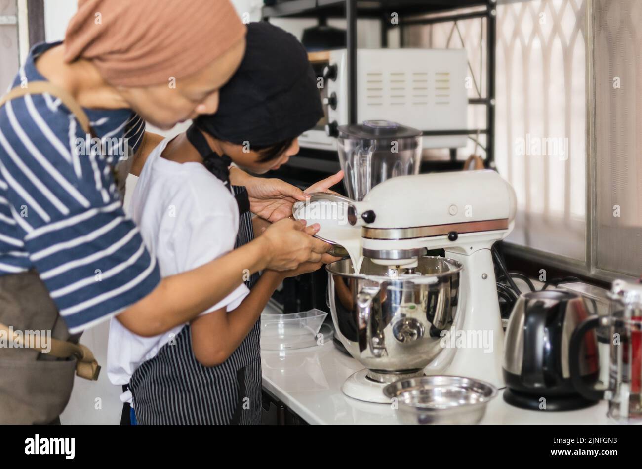 Mother teaching her son baking cake by pouring milk into a mixing bowl ...