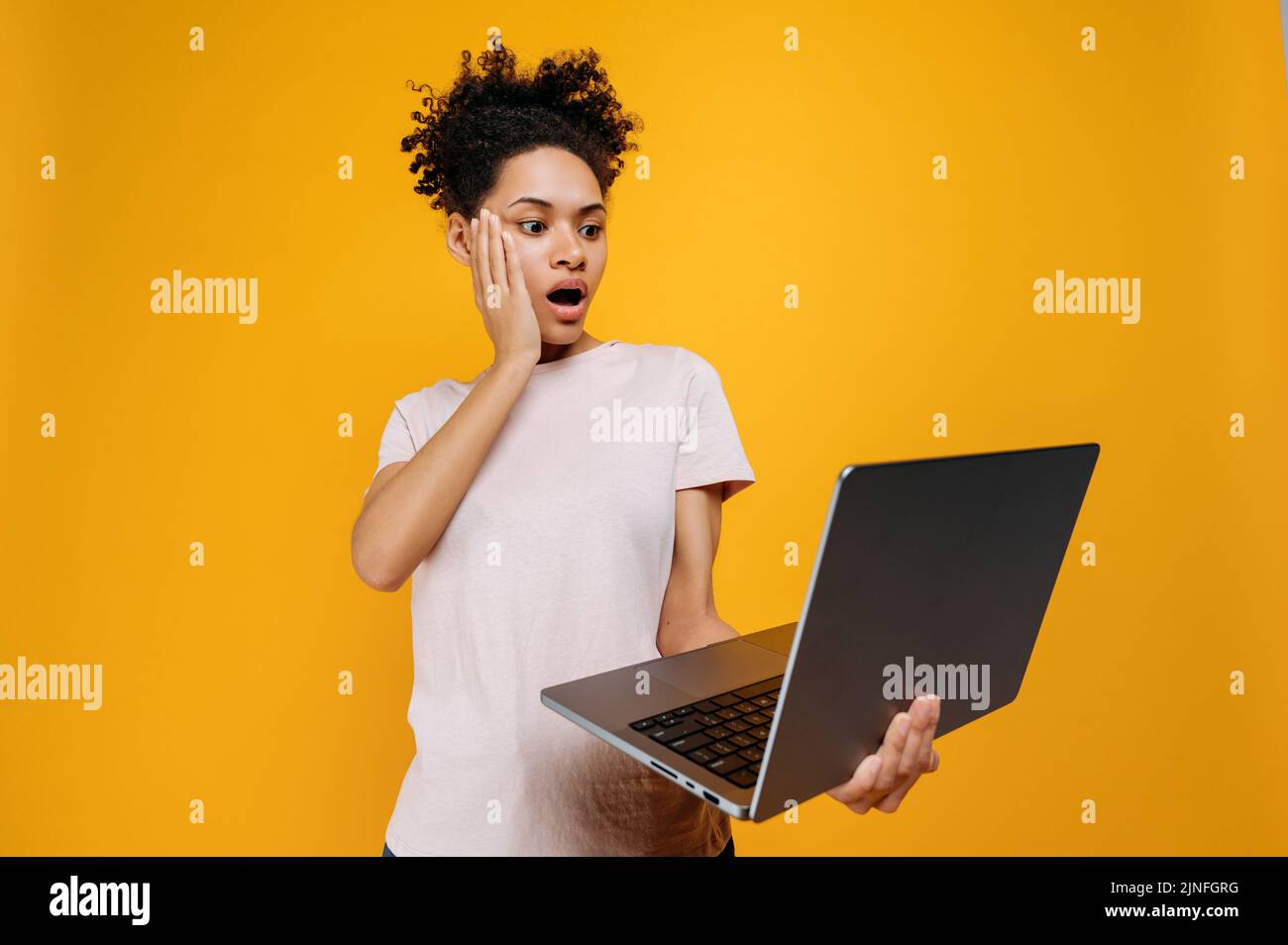 Surprised african american young woman with curly hair, holds an open ...
