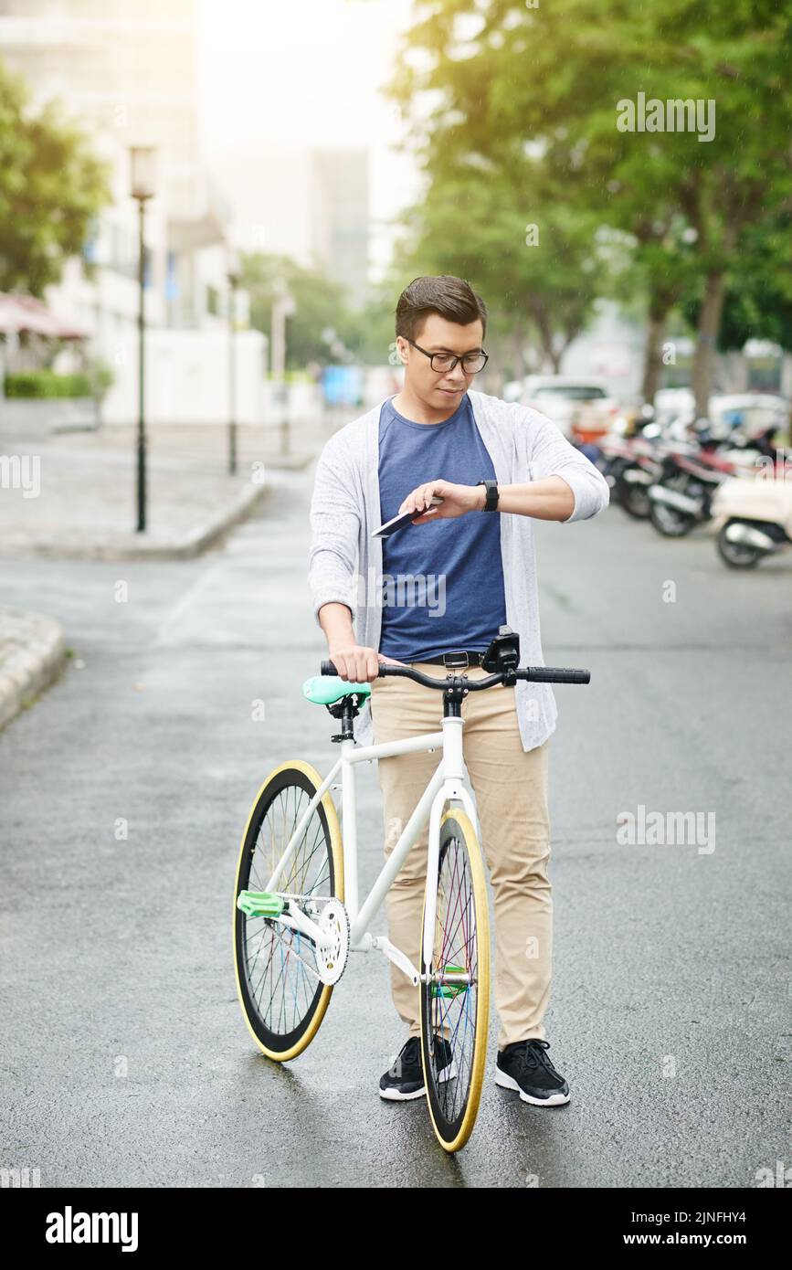 Young Asian man with bicycle checking information in his smartwatch ...