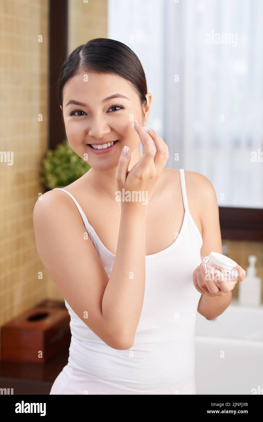 Cheerful young Asian woman applying hydration lotion on her face Stock ...