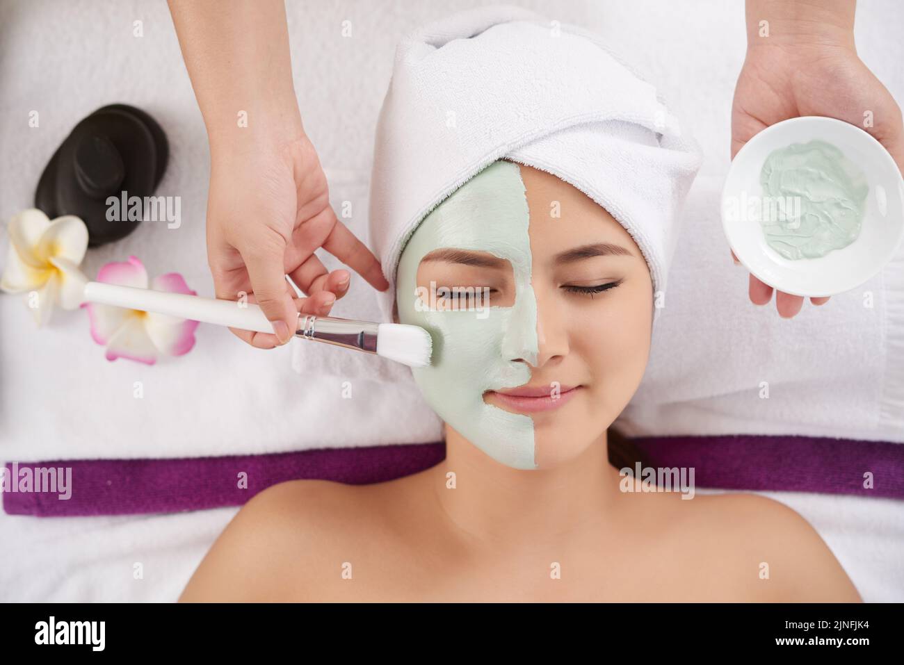 Beautician applying clay mask on face of pretty Vietnamese woman Stock ...