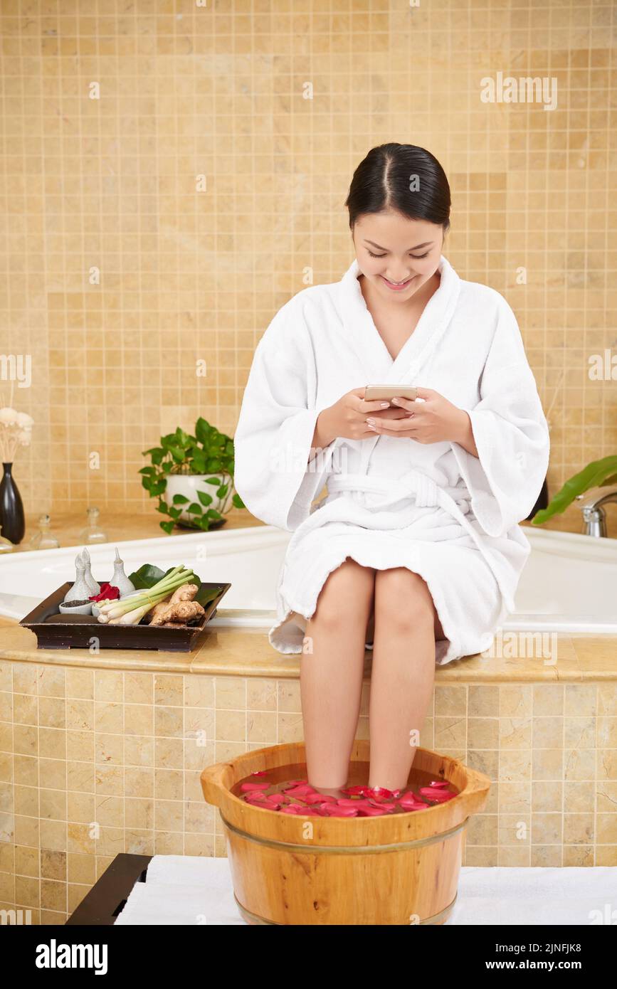 Woman texting when sitting with her feet in wooden basin with rosa ...
