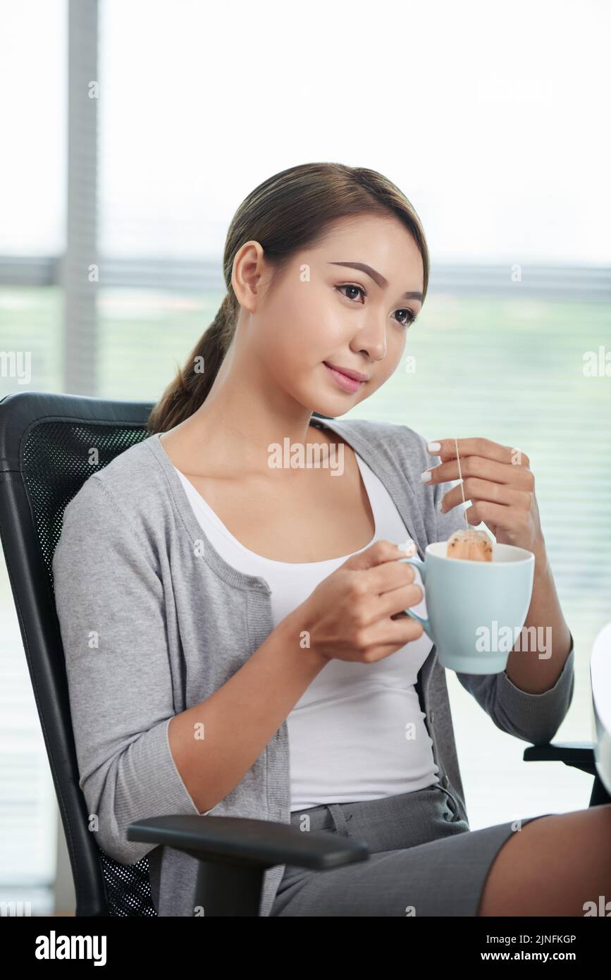 Portrait of pensive female entrepreneur drinking tea at her workplace ...