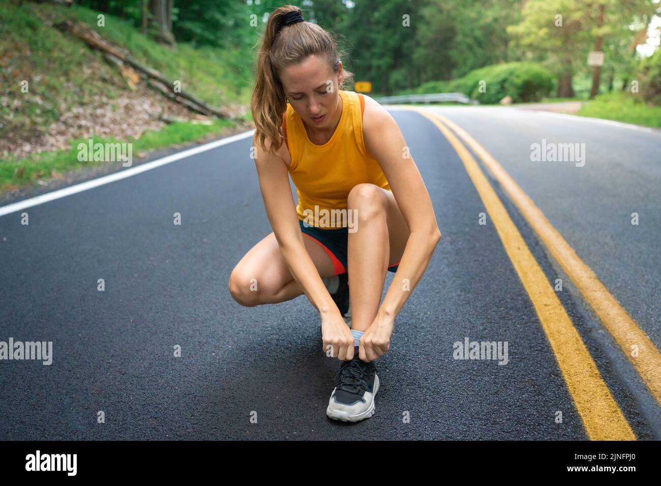 Runner woman tying laces for jogging run on forest road. Female athlete ...