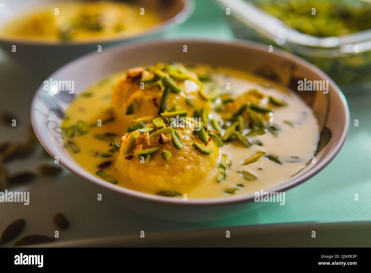 A bowl of freshly made kesar rasmalai on a table next to other dishes ...