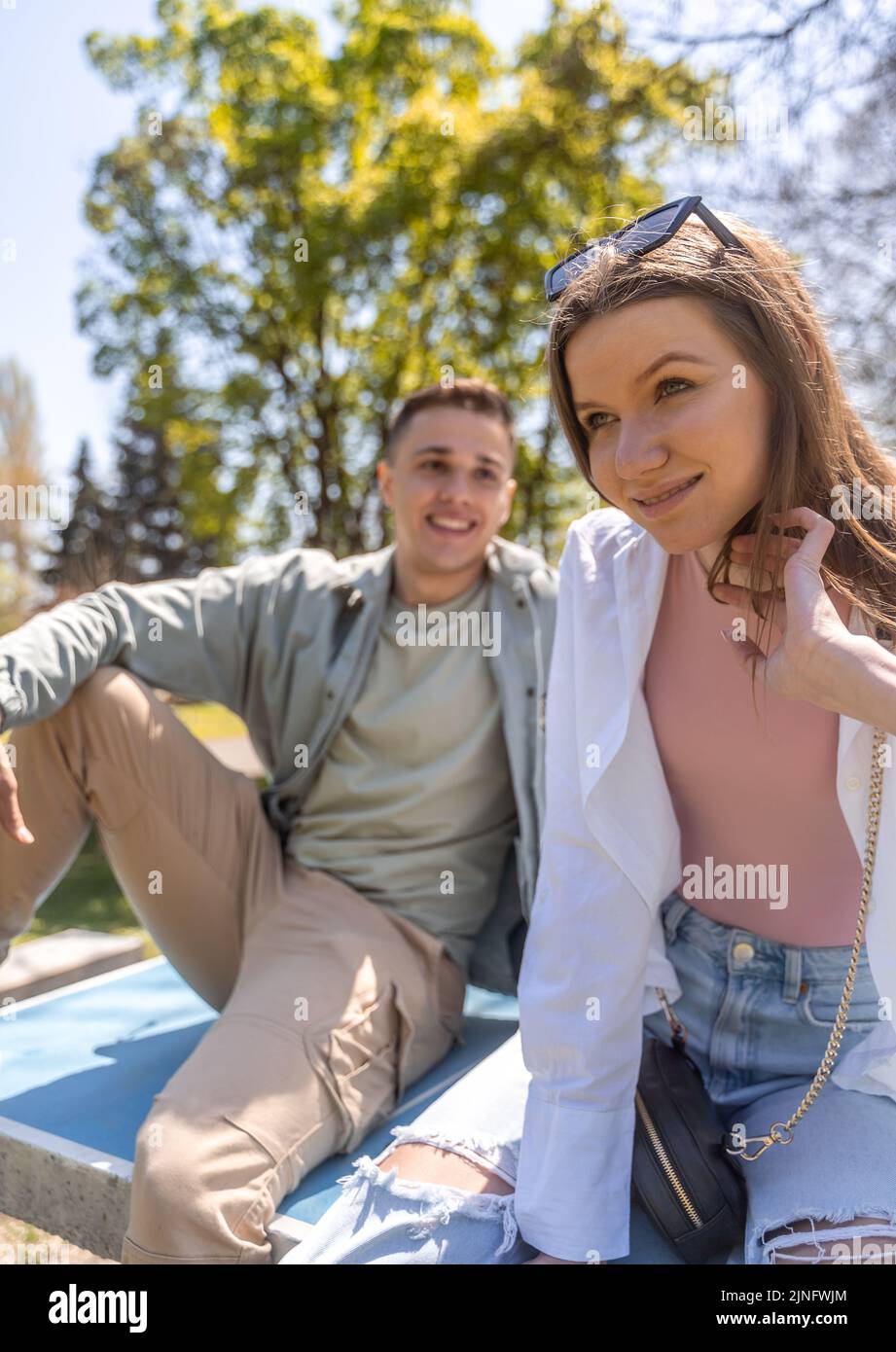 Friends or couple laughing and taking a conversation sitting on a bench ...