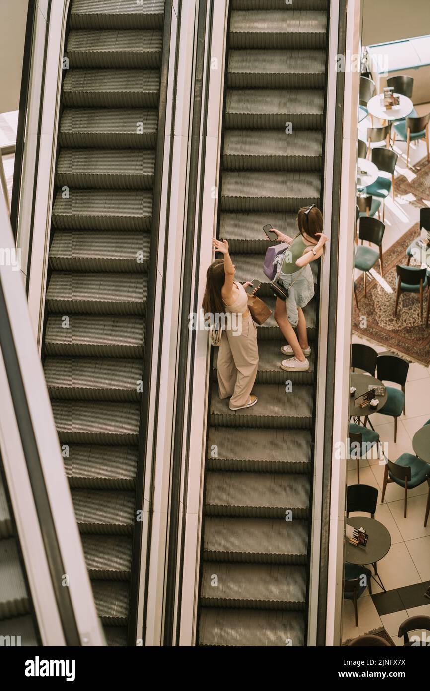 Two pretty girls going up on the escalator in the city mall while ...