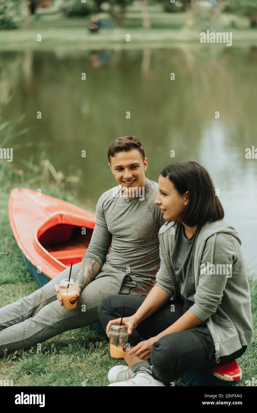 Pretty couple talking while sitting on a kayak in the park drinking ...