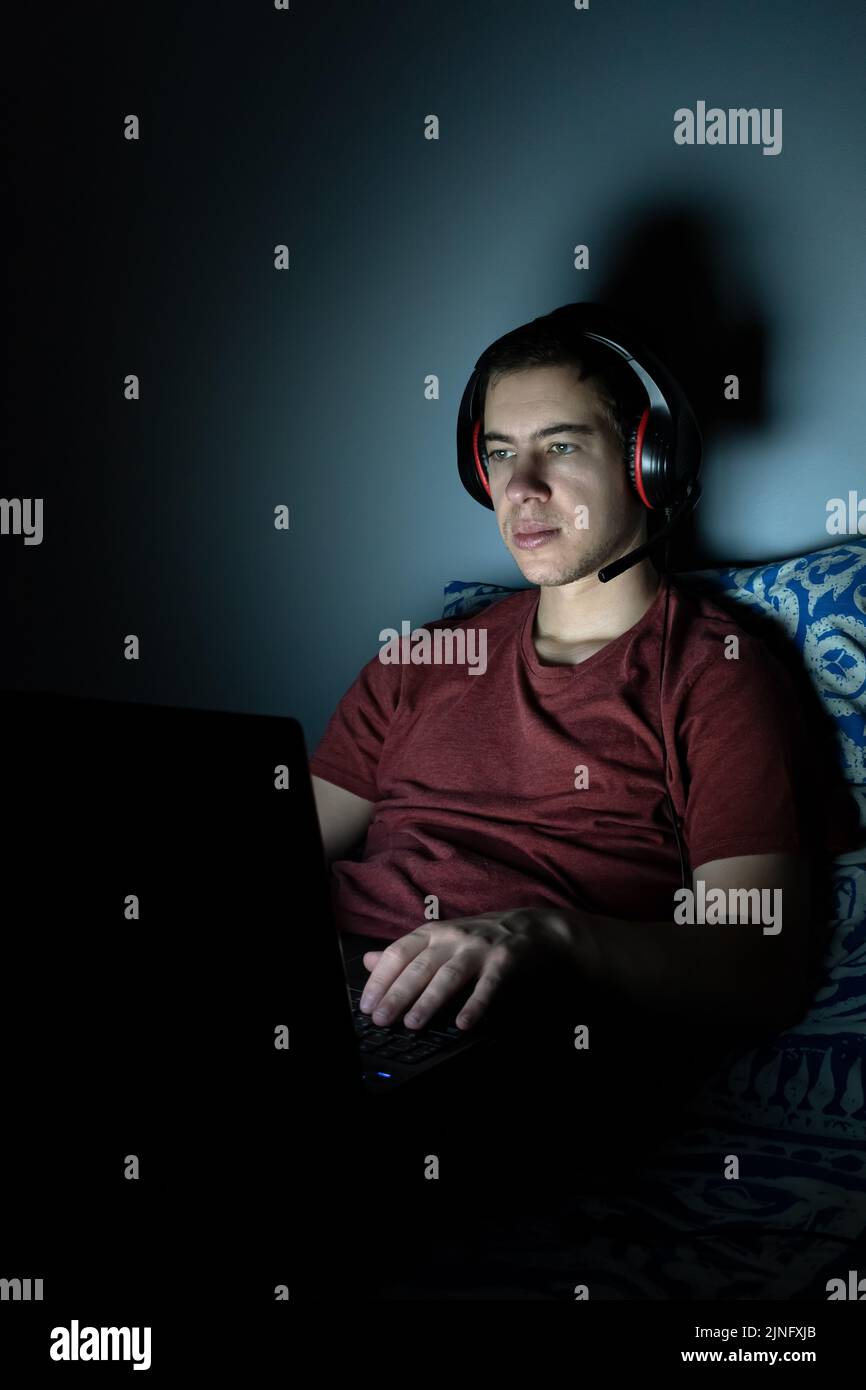 Millennial on the bed with the light off playing video games on the pc ...