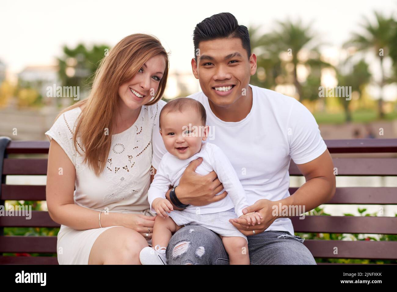 Cheerful smiling multi-ethnic family with baby boy sitting on bench ...