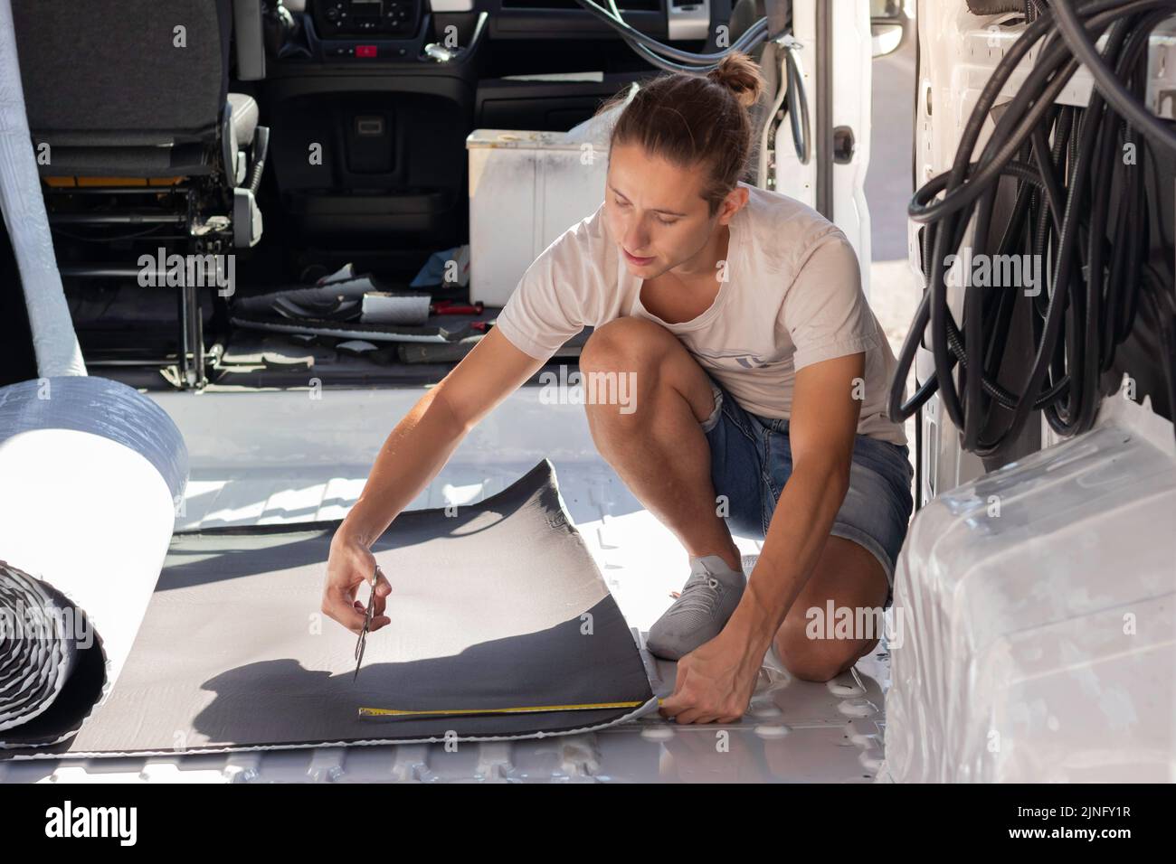 Young hipster man crouched measuring and cutting the roll isolation for ...