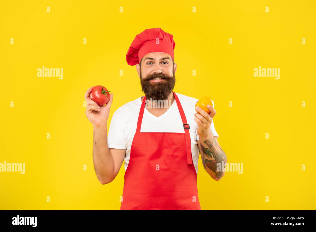 Happy man in cooking apron and toque holding red and yellow tomatoes ...