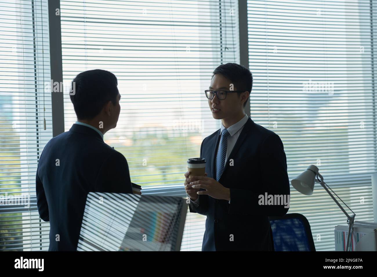 Young Vietnamese businessman with take-out coffee talking to coworker ...