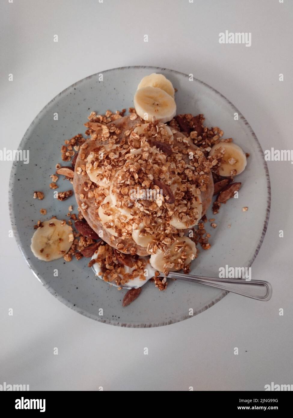 A vertical top view of a pancake with sliced bananas and oatmeal seeds ...