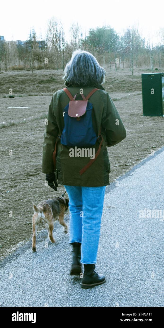 A woman in a khaki jacket with a backpack walking her dog, back view ...